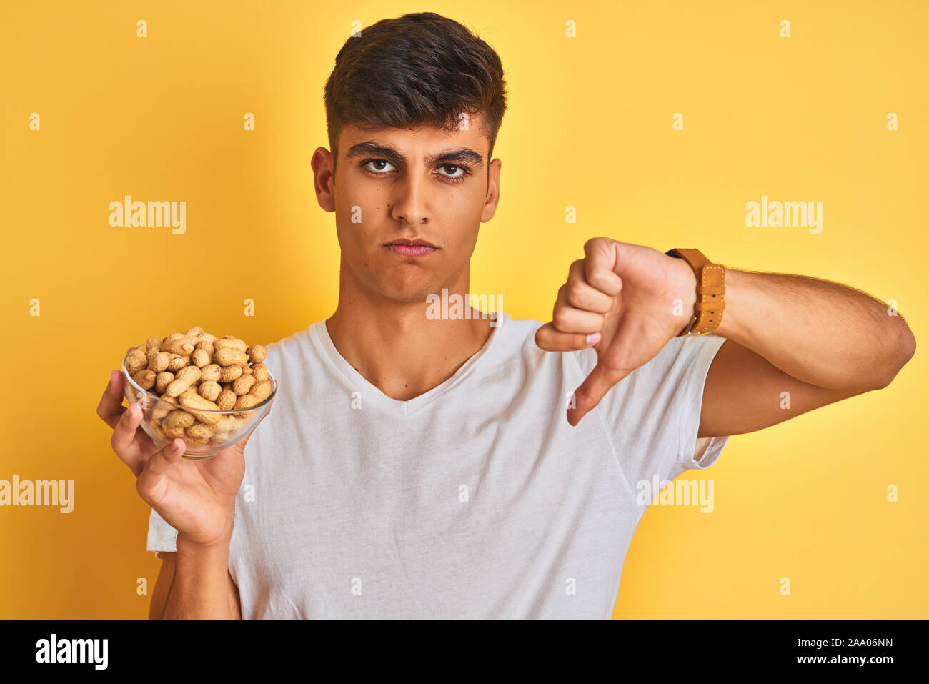Young indian man holding bowl with peanuts over isolated yellow ...