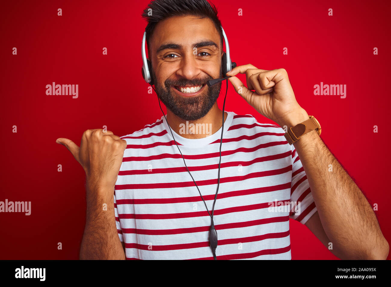 Young indian call center agent man using headset over isolated red ...