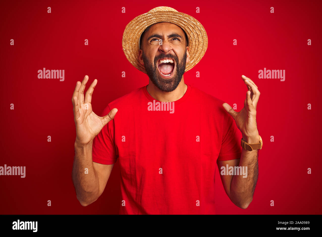 Young handsome indian man wearing t-shirt and hat over isolated red ...