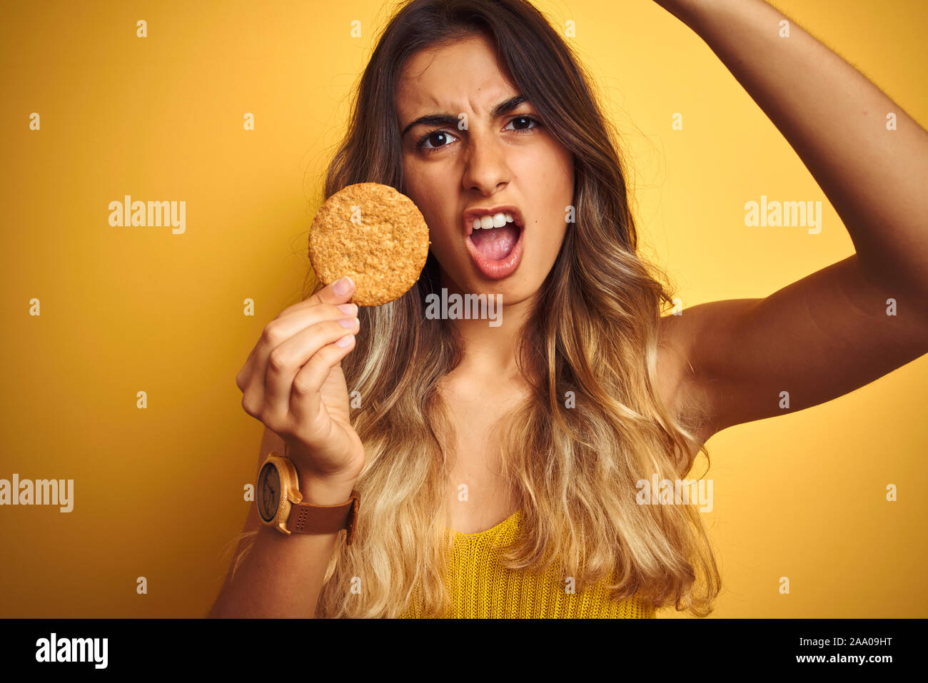 Young beautiful woman eating biscuit over grey isolated background ...