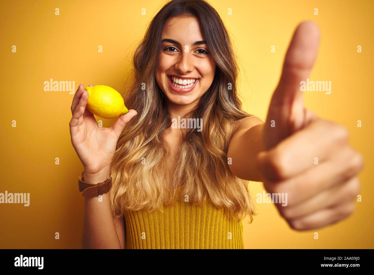 Young beautiful woman eating a lemon over yellow isolated background ...