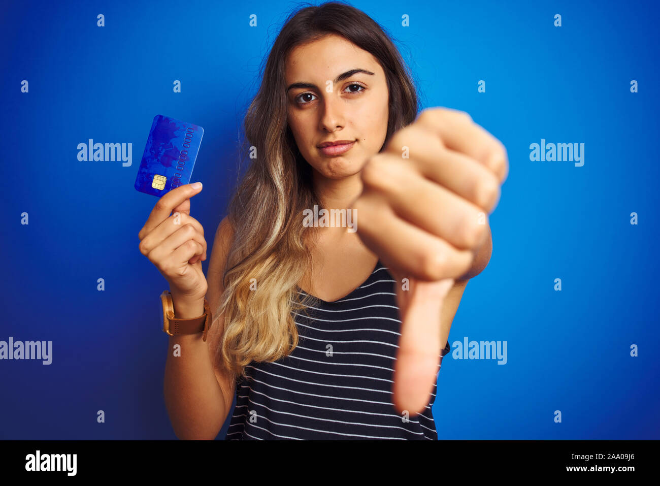 Young beautiful woman holding credit card over blue isolated background ...