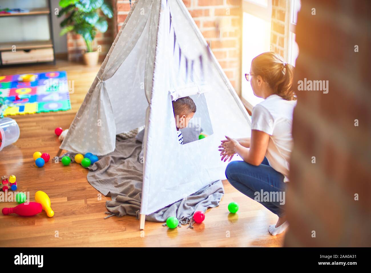 Beautiful teacher and toddler boy sitting on the floor playing inside ...