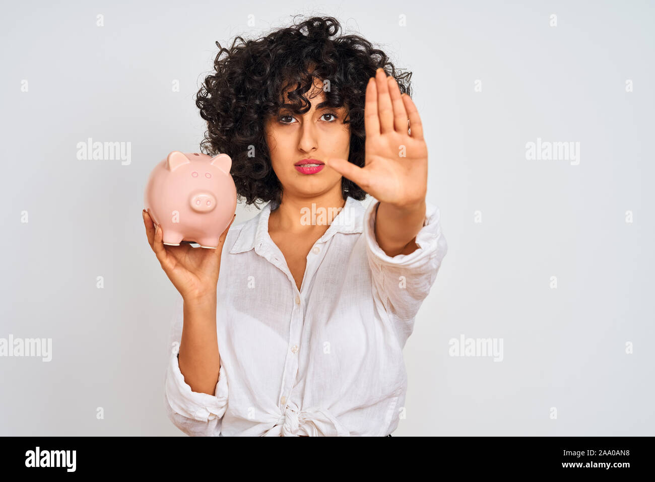 Young arab woman with curly hair holding piggy bank over isolated white ...