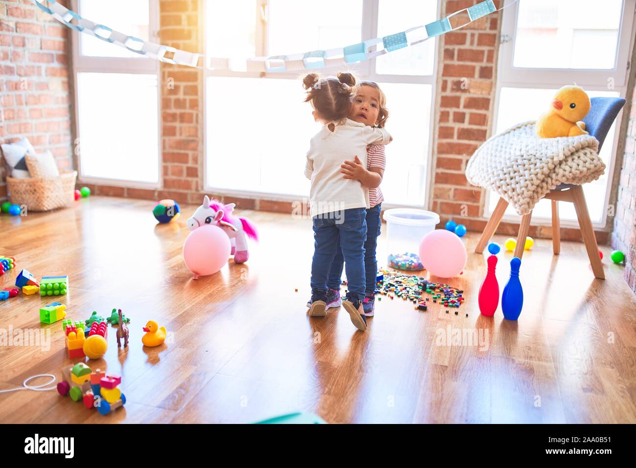 Adorable toddlers hugging standing around lots of toys at kindergarten ...