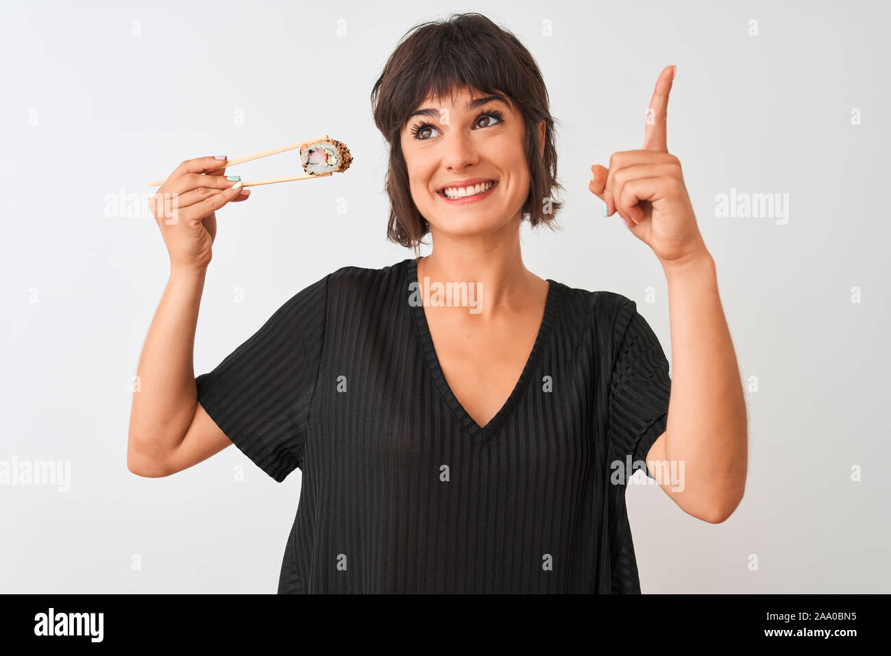 Young beautiful woman eating sushi using chopsticks standing over ...