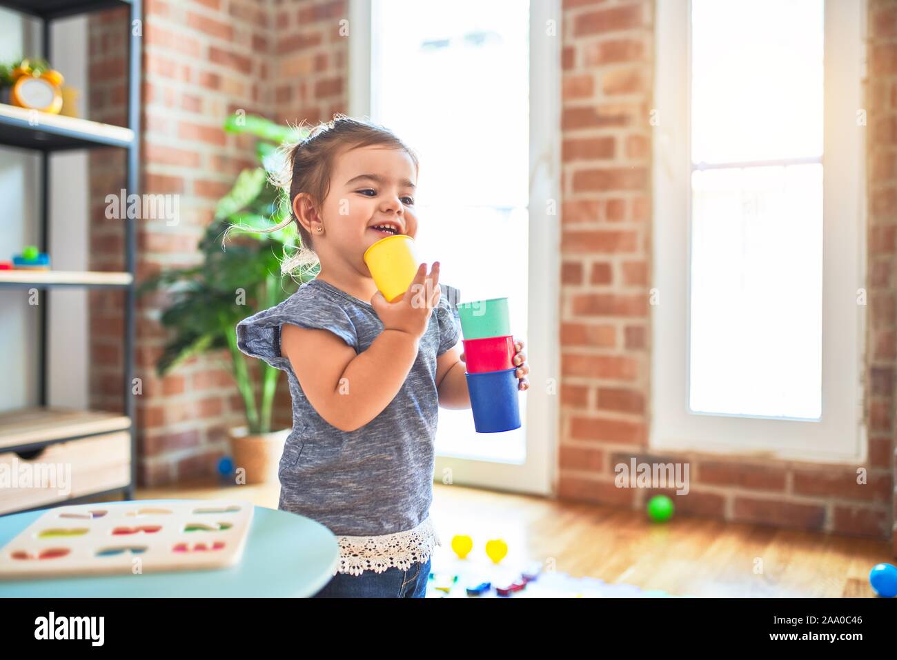Beautiful toddler standing playing with colorful plastic cups at ...