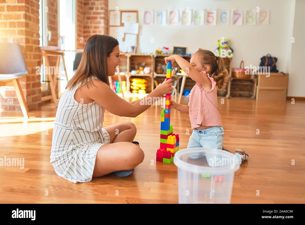 Beautiful teacher and blond toddler girl building tower using plastic ...