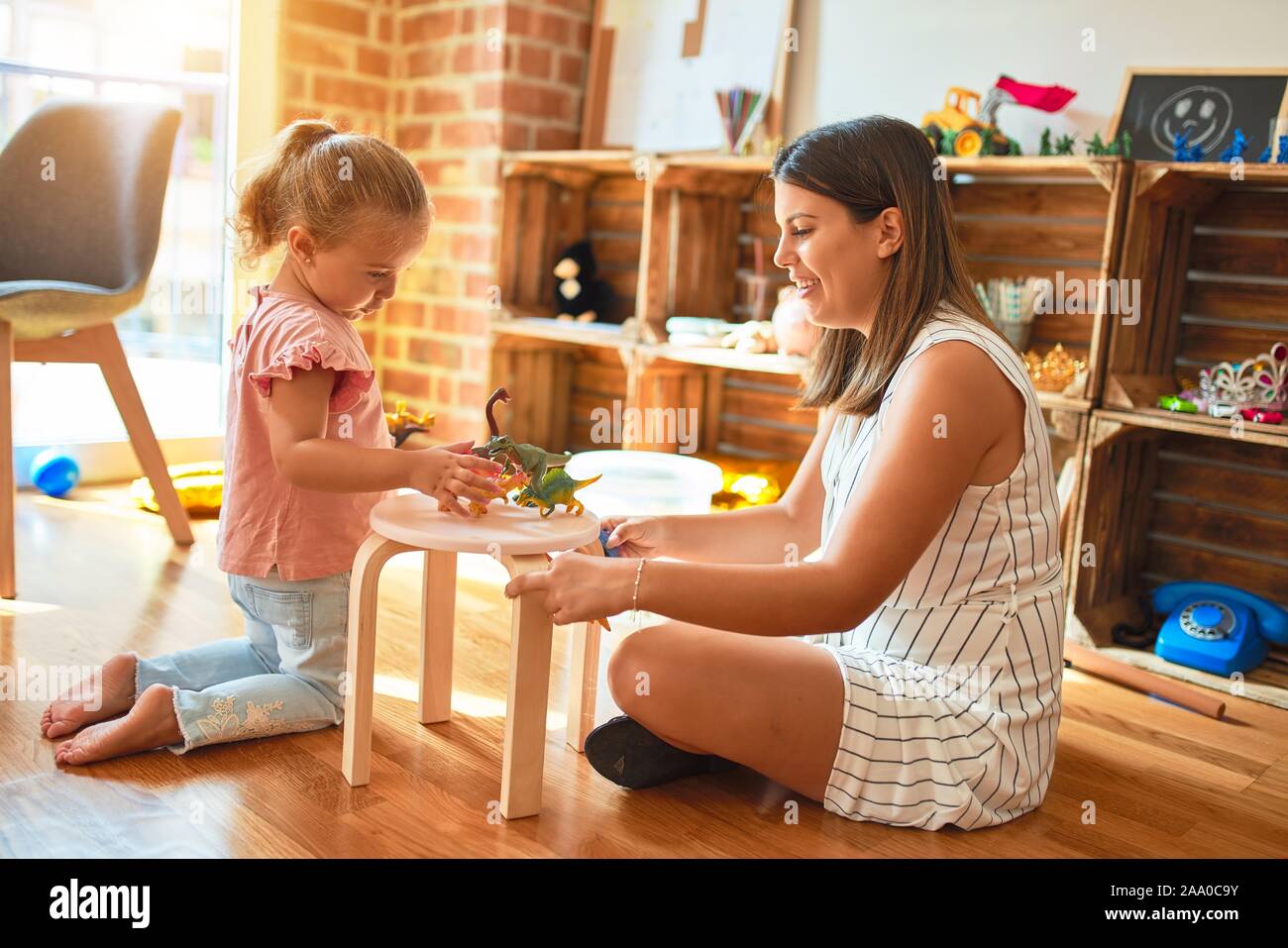 Beautiful teacher and blond student toddler girl playing with dinosaurs ...