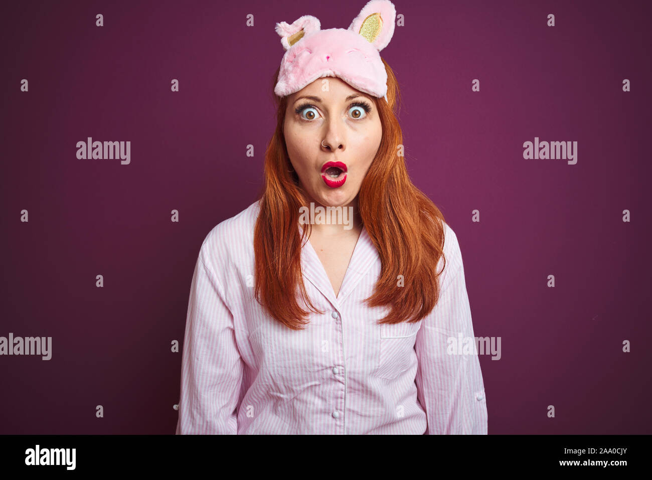 Young beautiful redhead woman wearing pajama and mask over purple ...