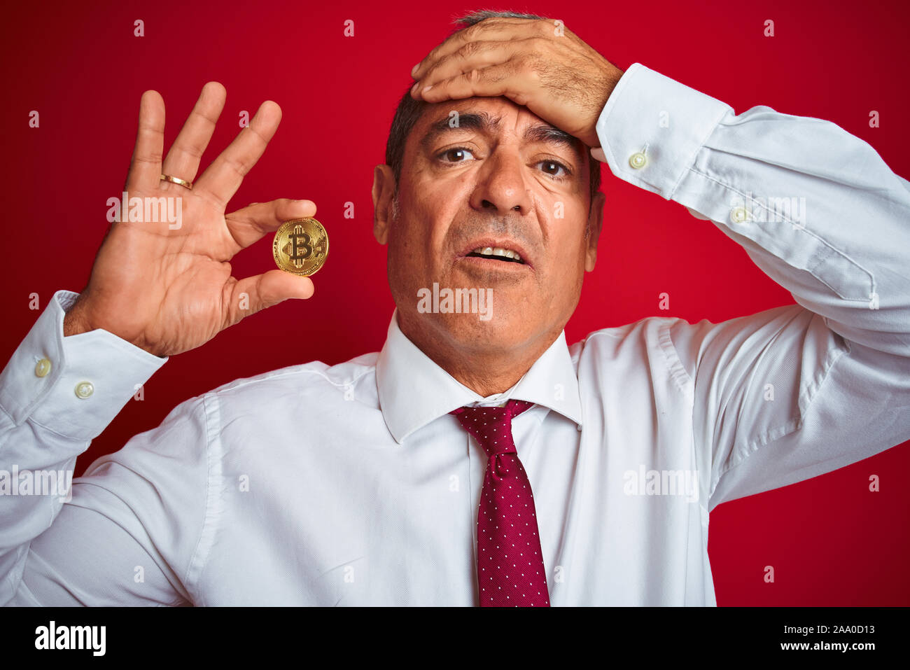 Handsome middle age man holding bitcoin standing over isolated red ...