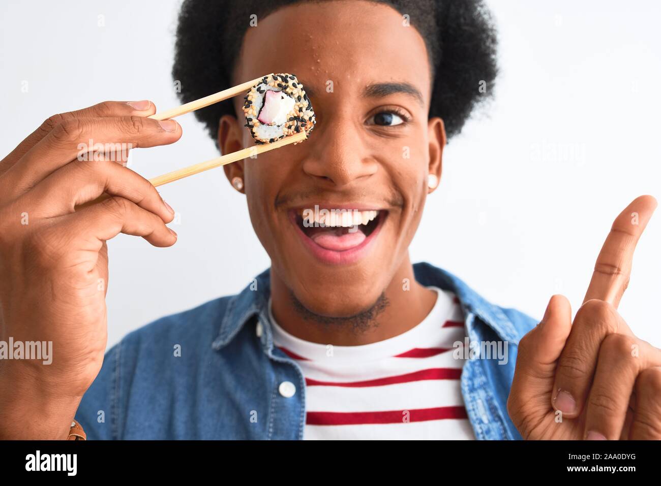 Young african american man eating sushi using chopsticks over isolated ...