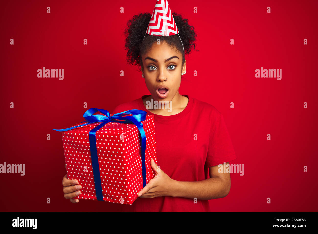 African american woman wearing funny hat holding birthday gift over ...
