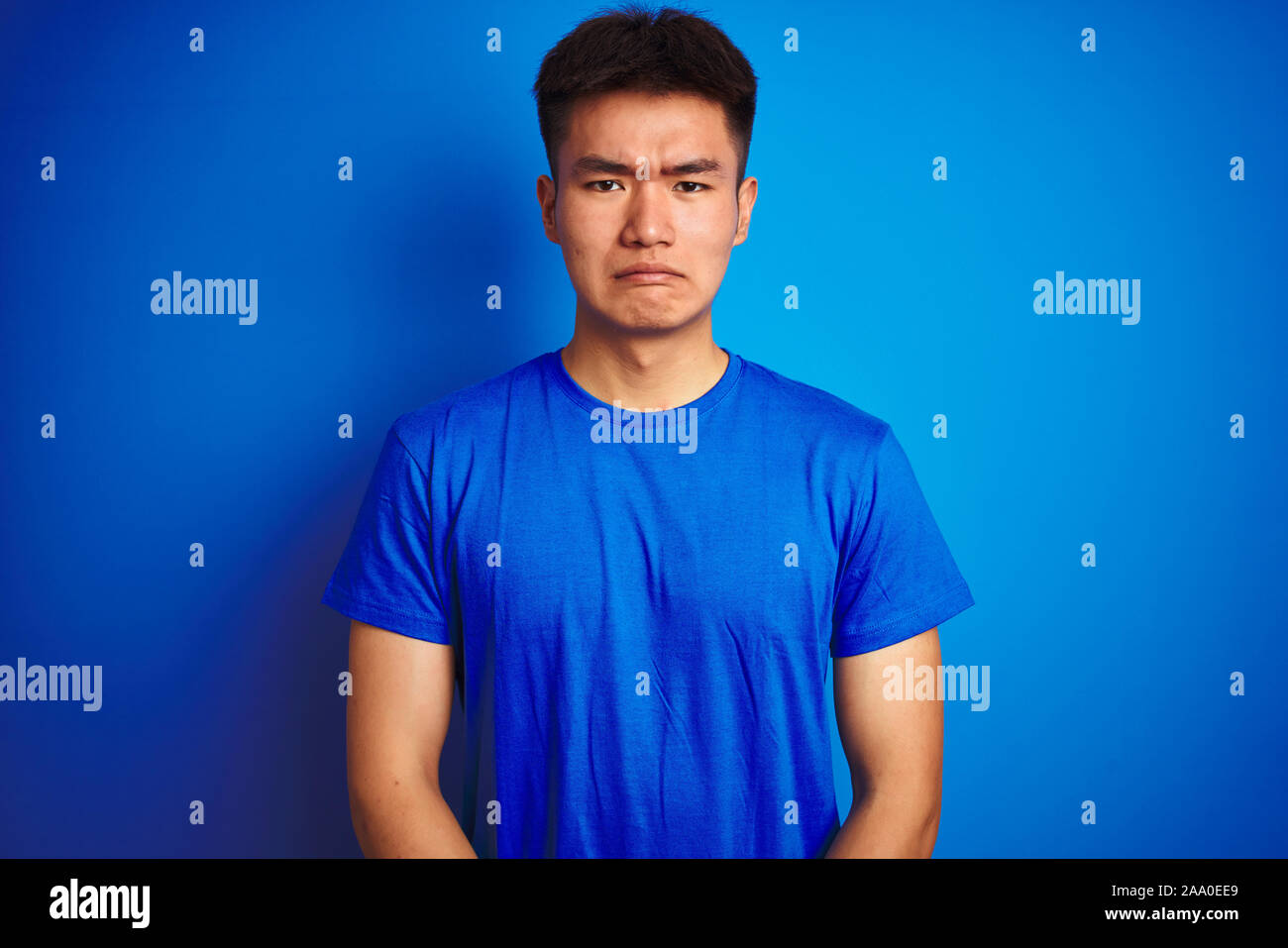 Young asian chinese man wearing t-shirt standing over isolated blue ...