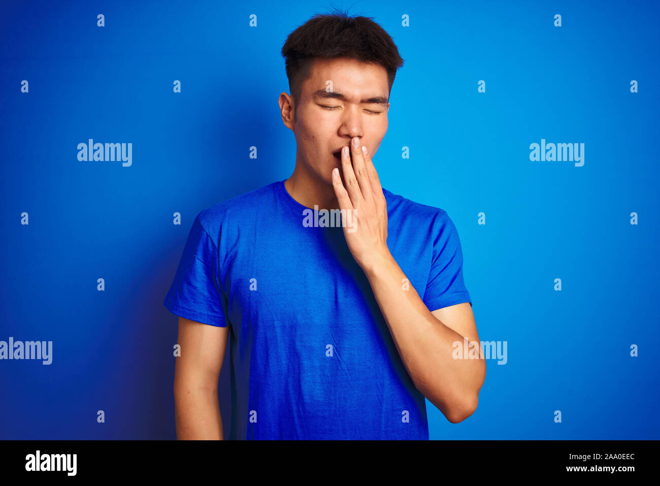 Young asian chinese man wearing t-shirt standing over isolated blue ...