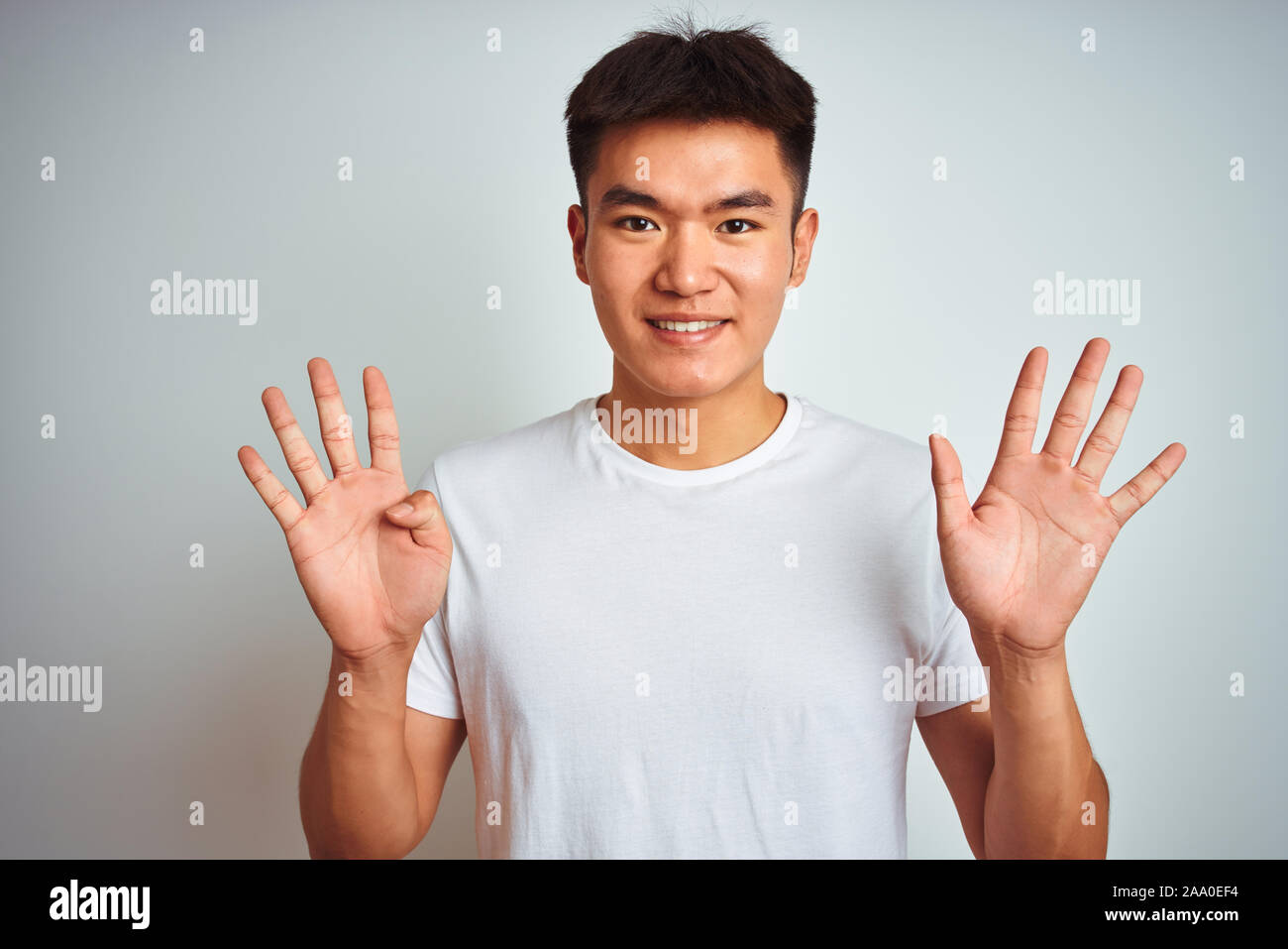 Young asian chinese man wearing t-shirt standing over isolated white ...