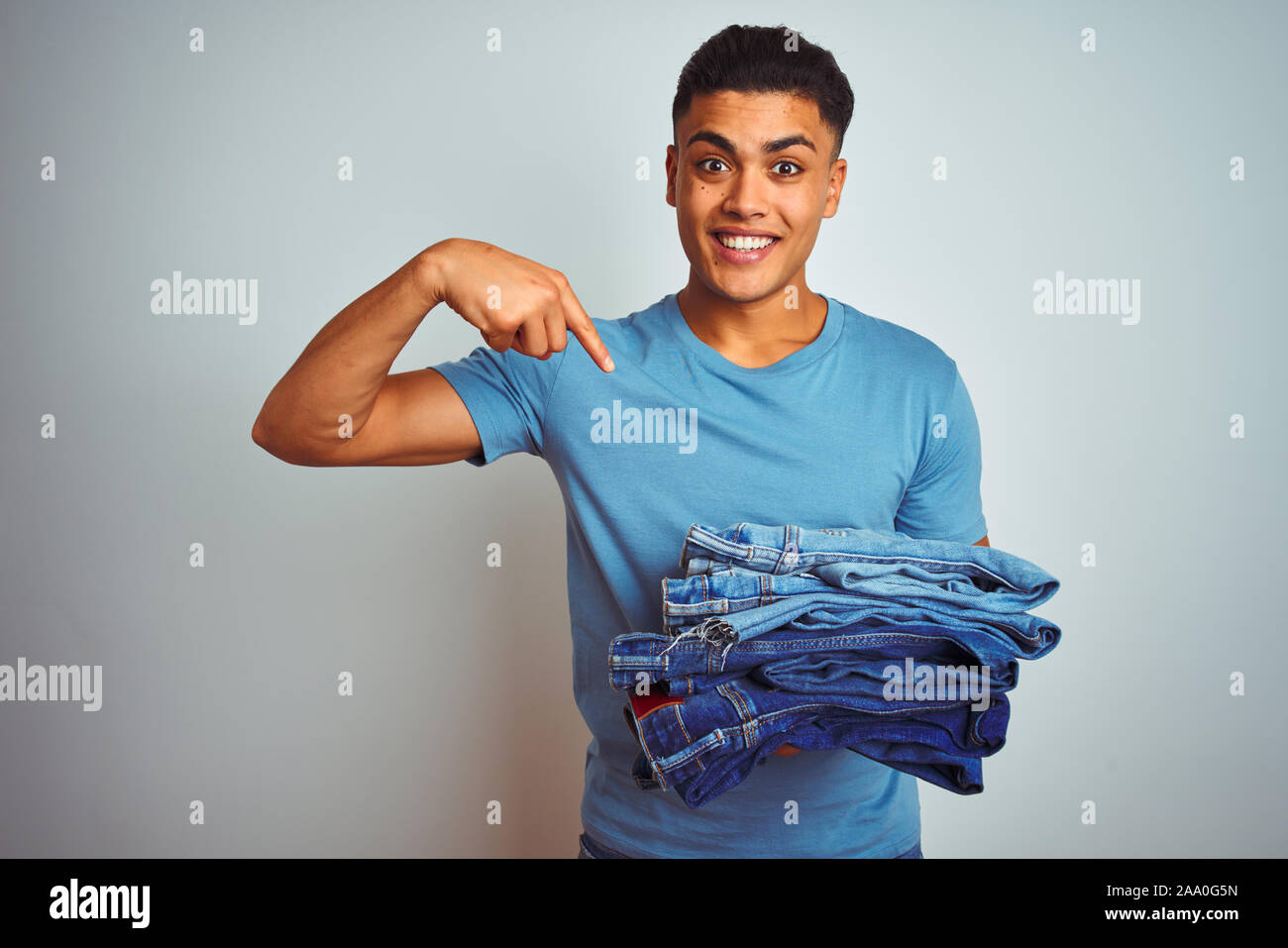 Young brazilian shopkeeper man holding jeans standing over isolated ...