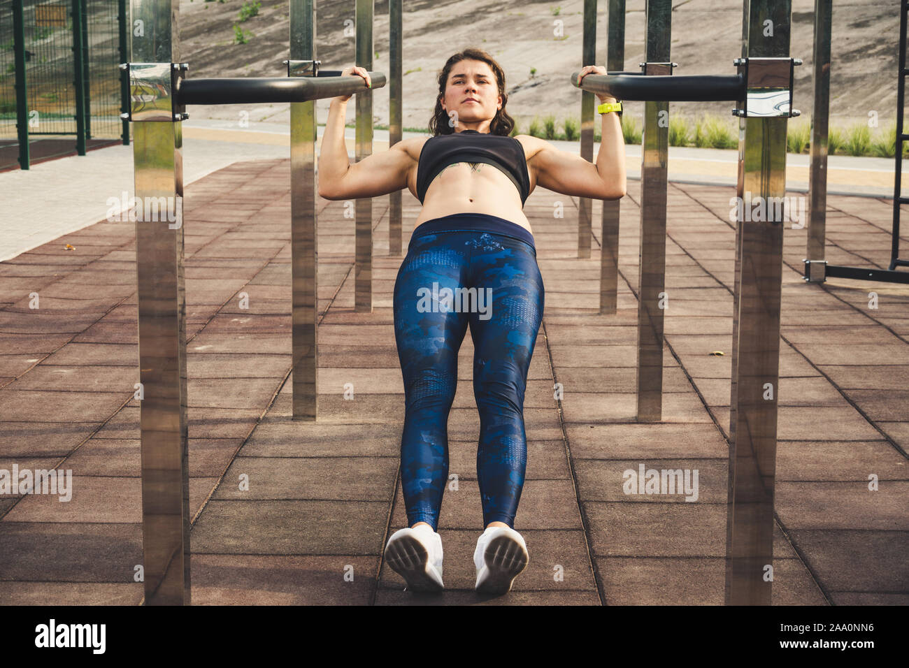 girl trains outdoors in street gym. Training of biceps and triceps ...