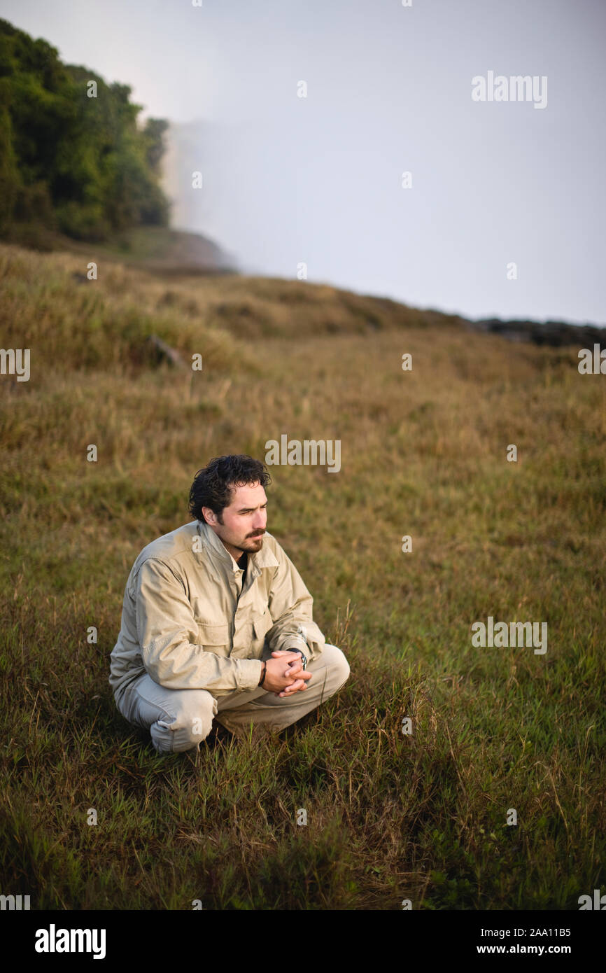 Mid-adult man crouching in grass near a waterfall Stock Photo - Alamy