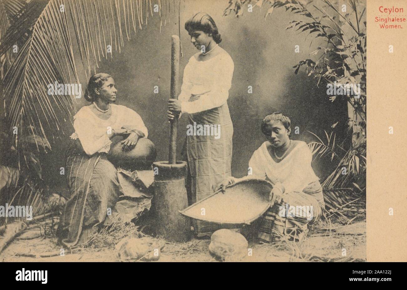 Monochrome postcard featuring three Singhalese women hulling rice in a ...