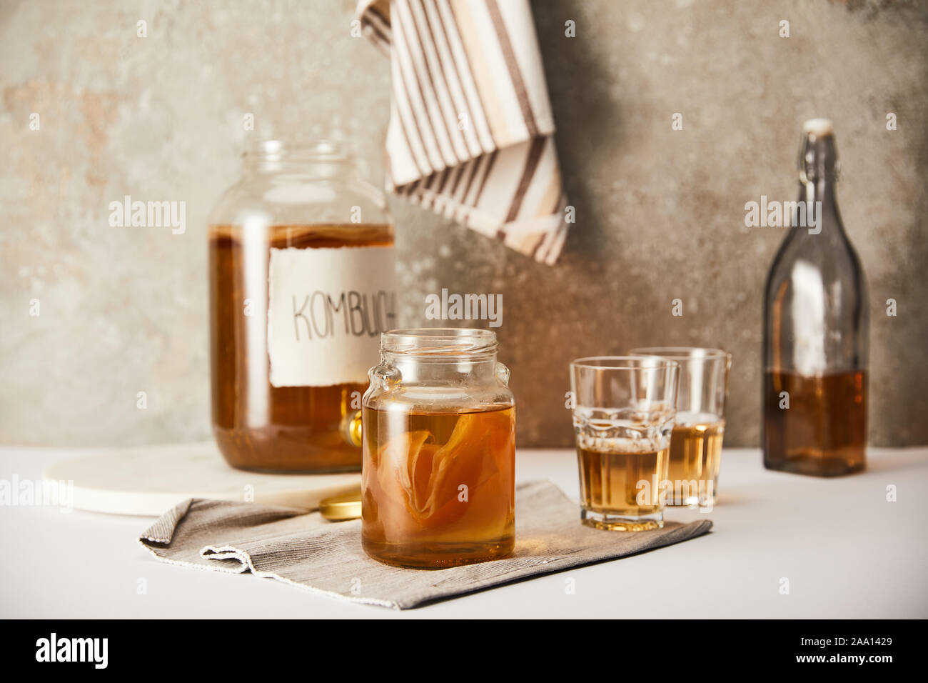 selective focus of jar with kombucha near glasses on textured grey ...