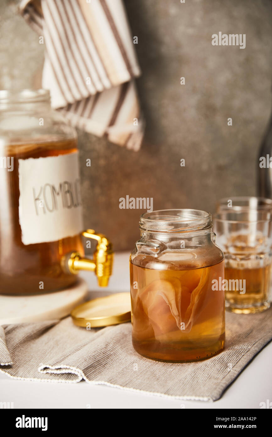 selective focus of jar with kombucha near glasses on textured grey ...