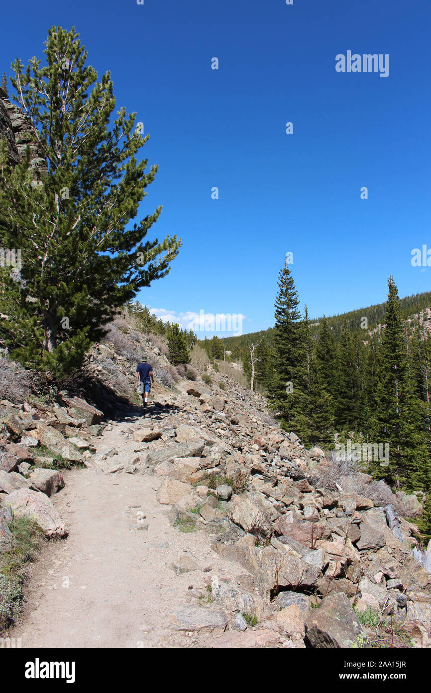 A young man walking along a rocky section of the Glacier Gorge Trail in ...