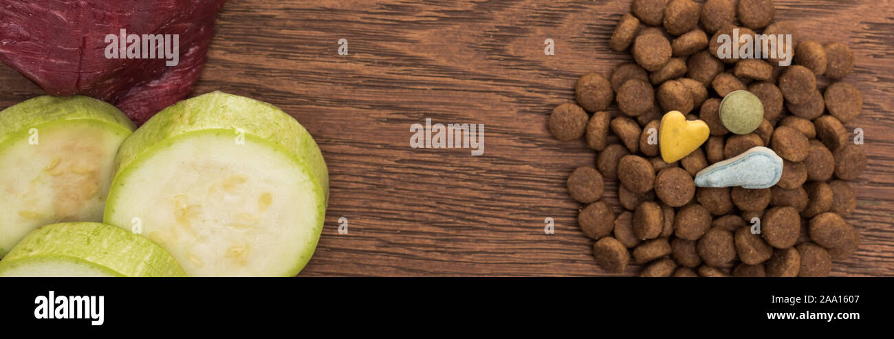 top view of raw meet, zucchini near vitamins on dry pet food on wooden ...