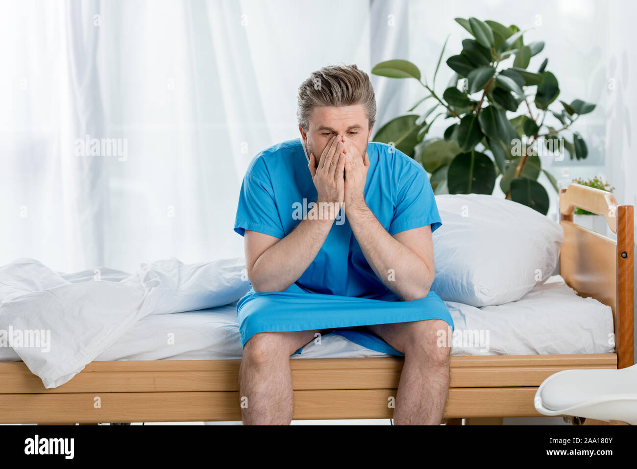 sad patient in medical gown sitting on bed and obscuring face in ...