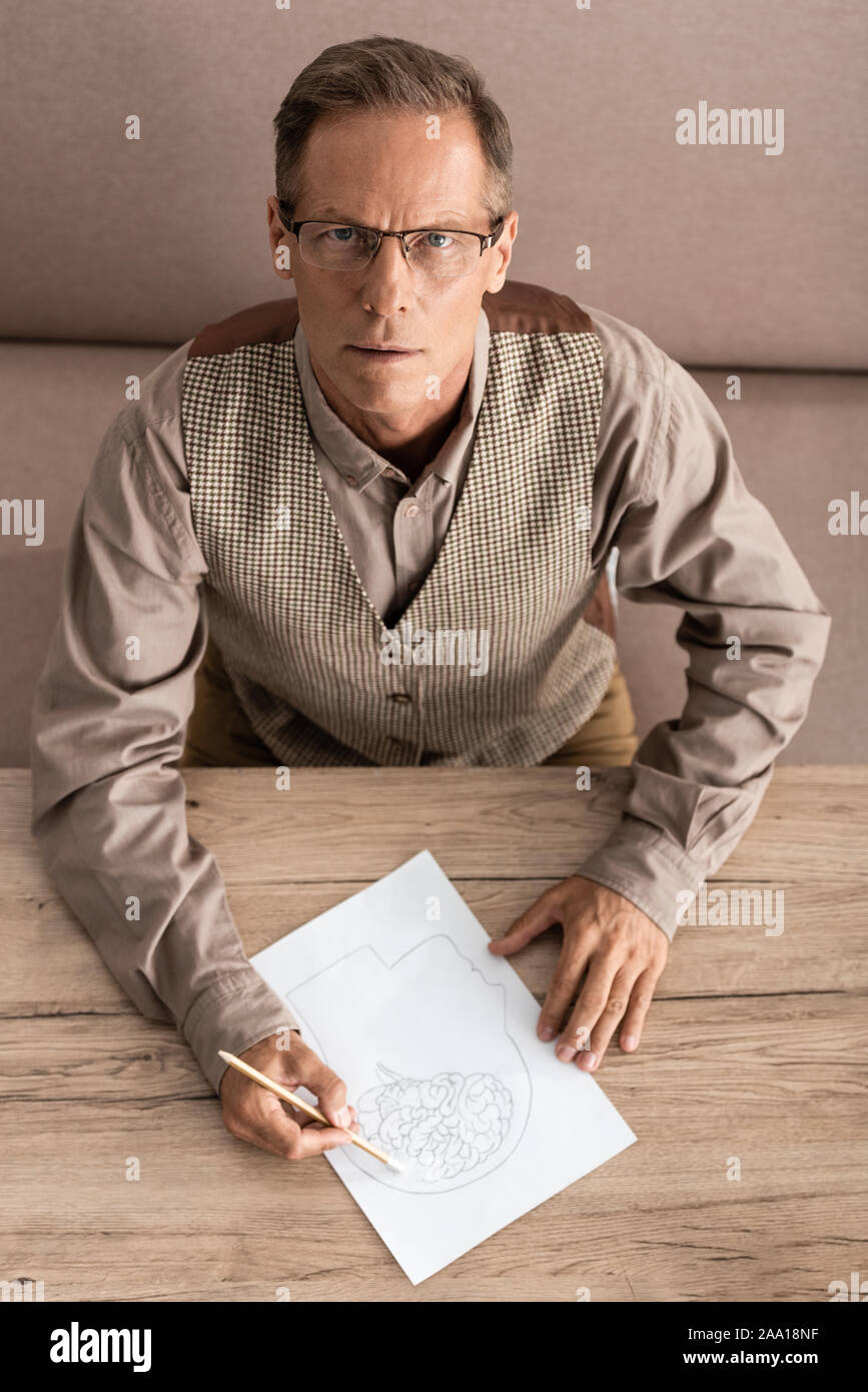 top view of senior man in glasses holding pencil while drawing picture ...
