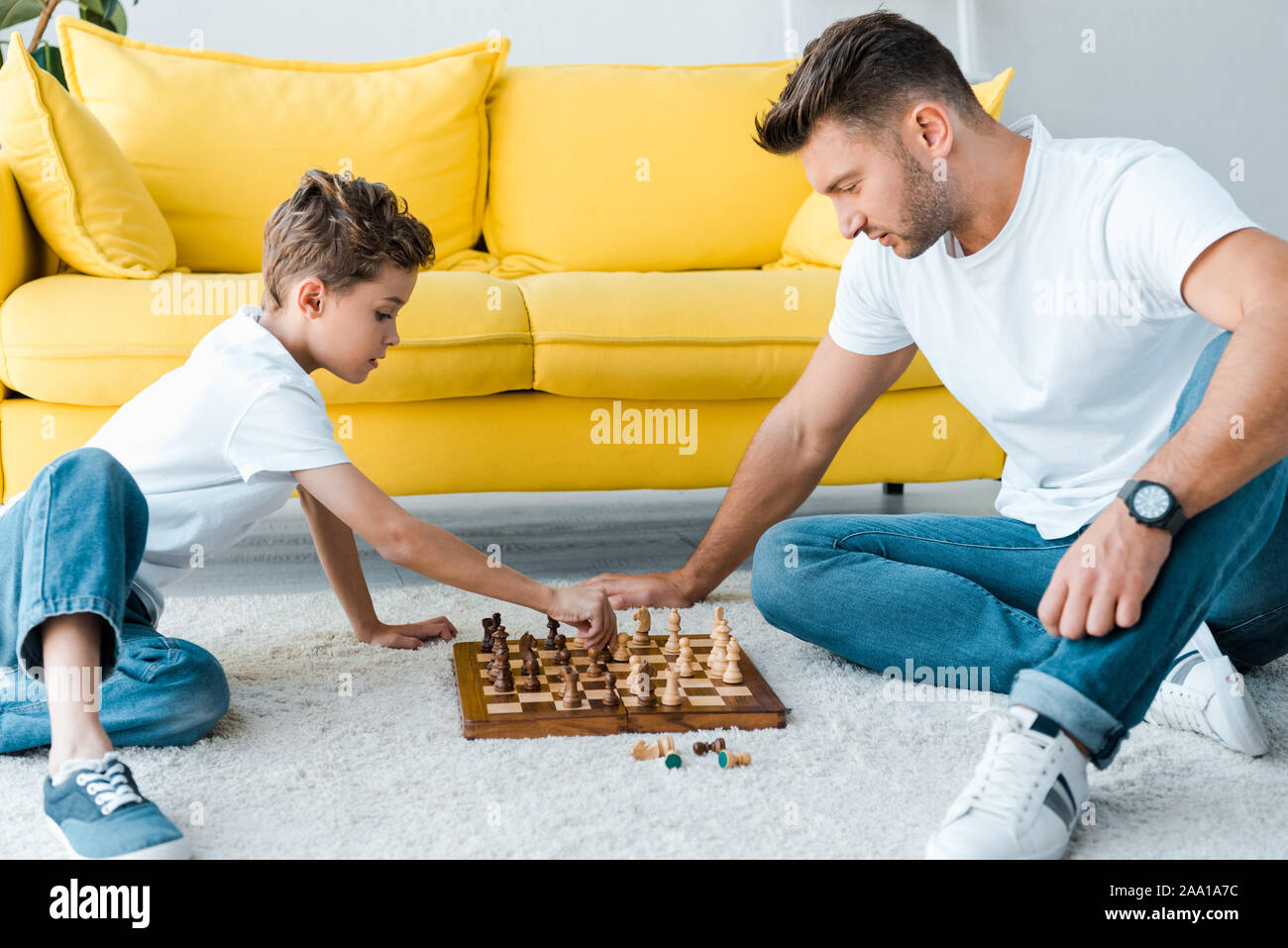 side view of handsome father and son playing chess on carpet Stock ...