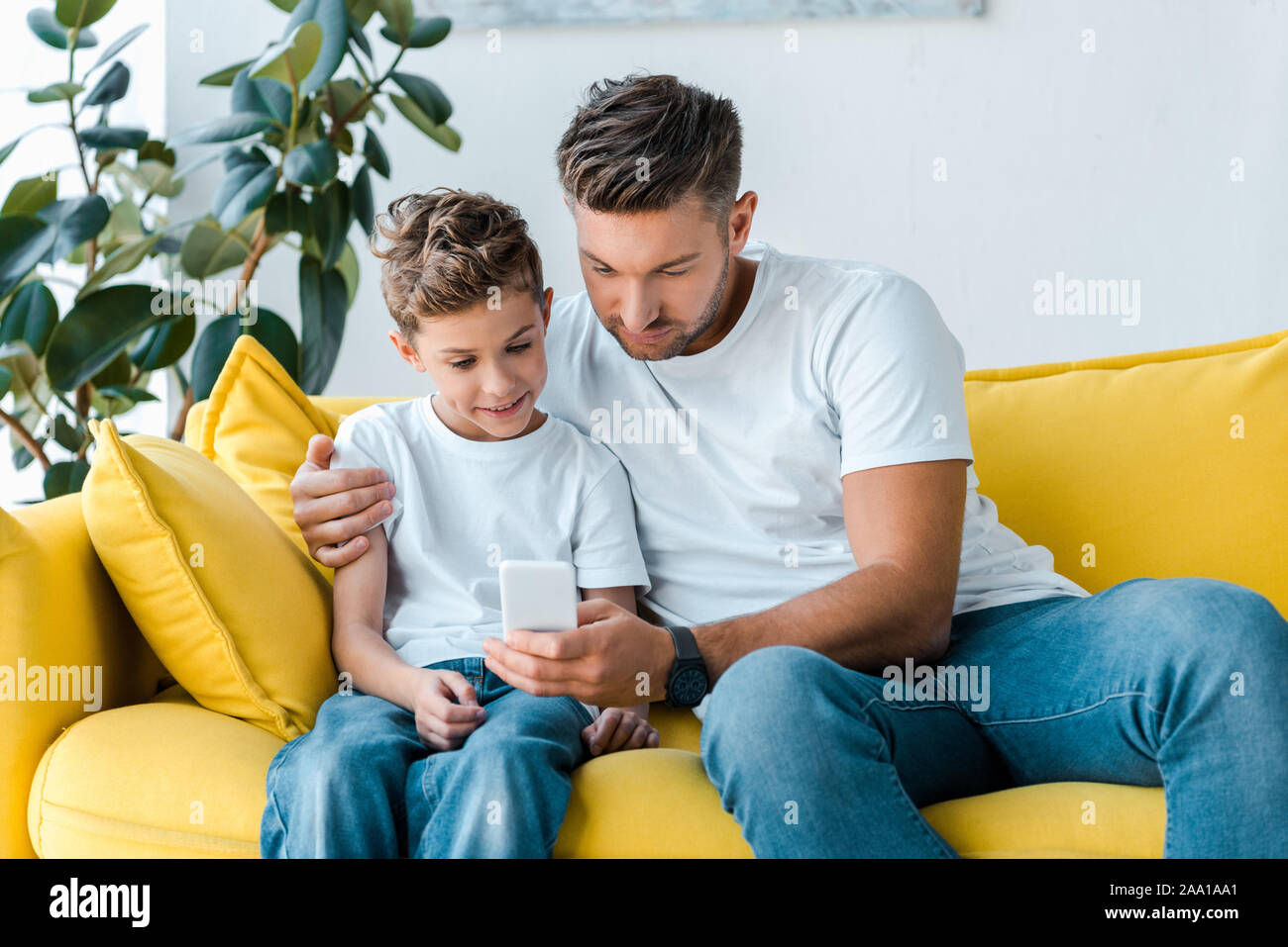 cute son and father looking at smartphone while sitting on sofa Stock ...
