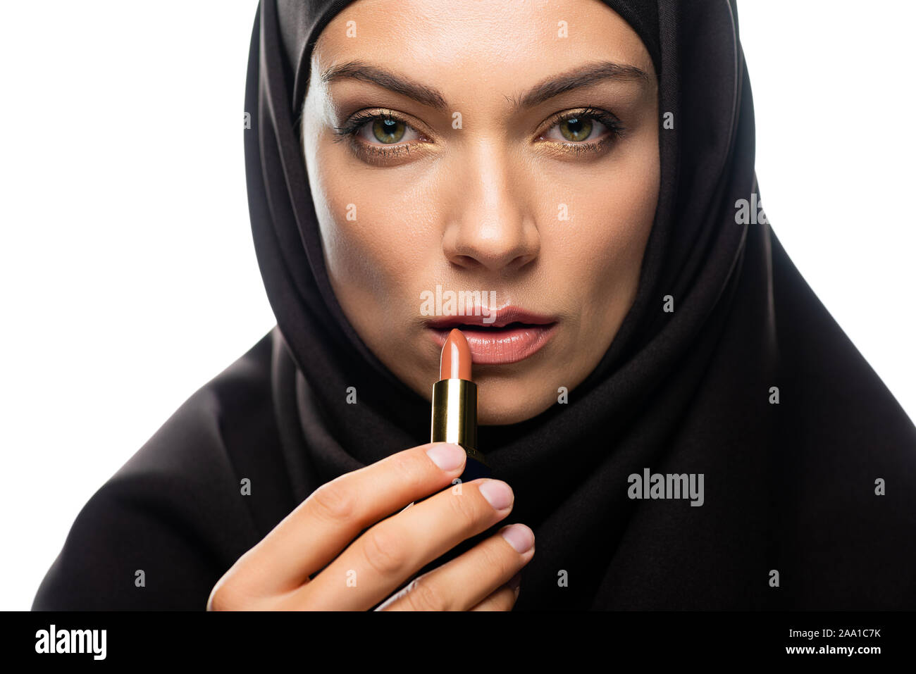 young Muslim woman in hijab applying beige lipstick isolated on white ...