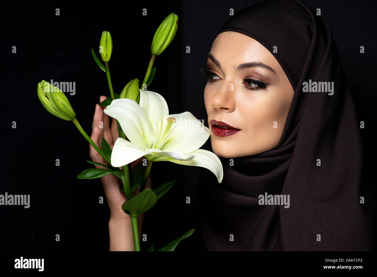 attractive Muslim woman in hijab with red lips holding lily isolated on ...