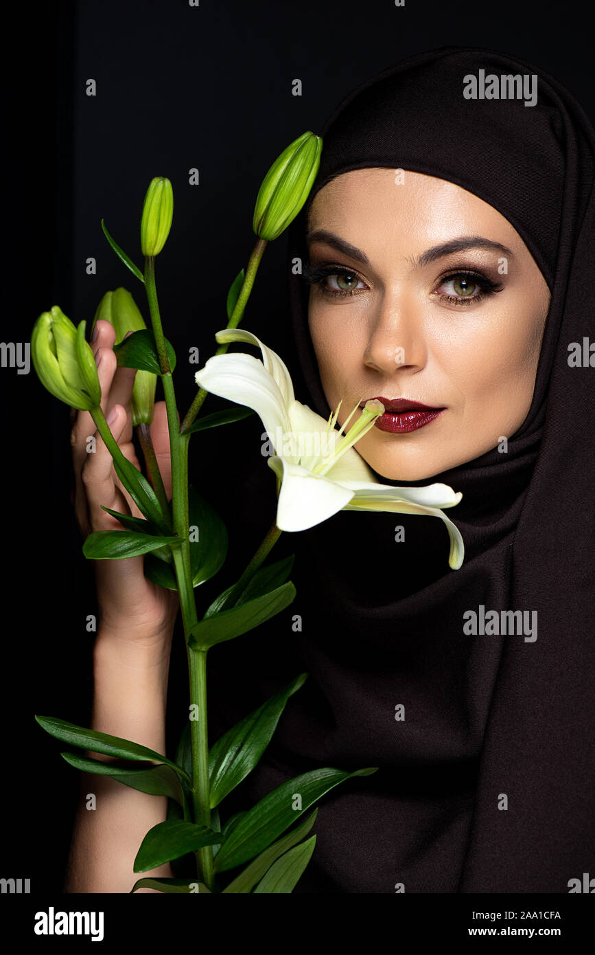 attractive Muslim woman in hijab with red lips holding lily isolated on ...