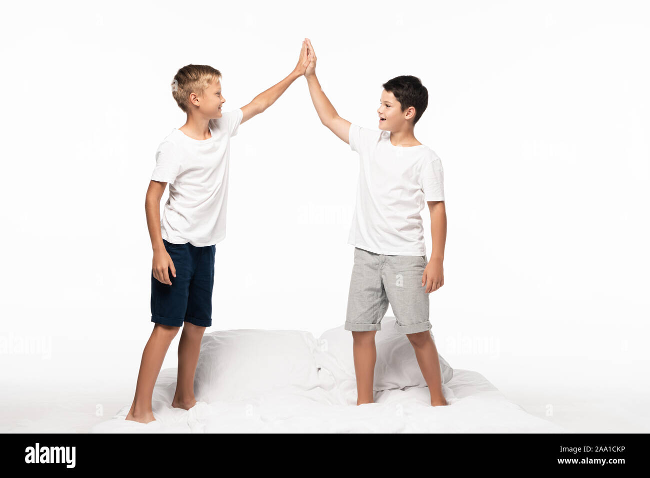 two happy brothers standing on bed and giving high five isolated on ...