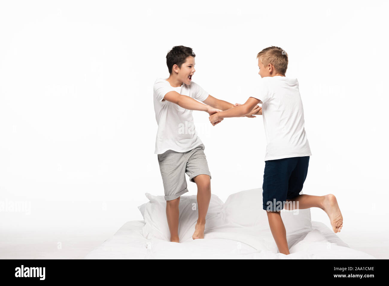 two brothers fighting for fun white standing on bed isolated on white ...