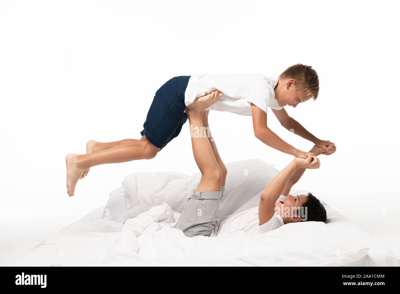 two cheerful brothers in pajamas having fun on bed isolated on white ...