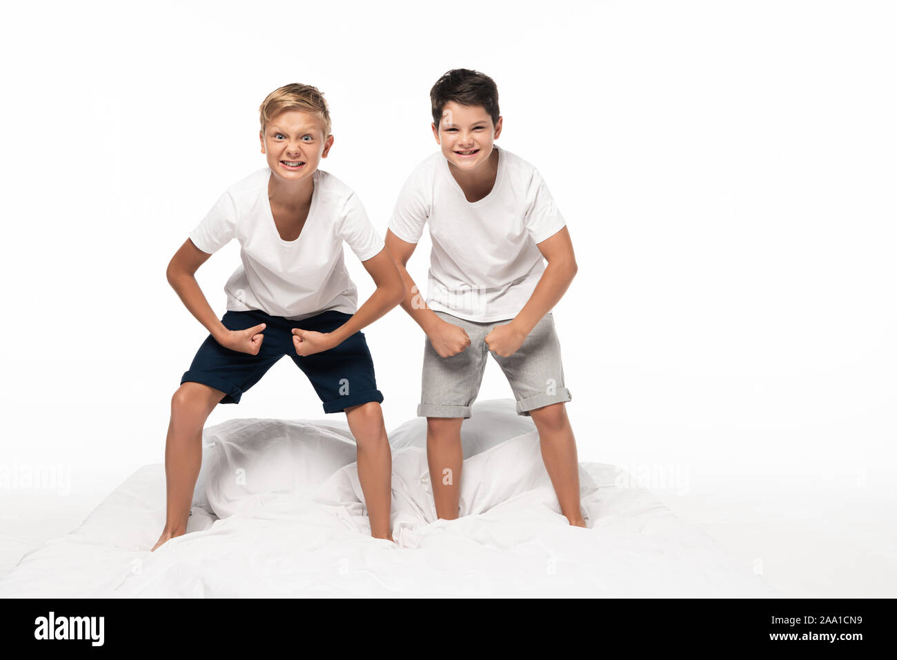 two cheerful brothers imitating bodybuilders while standing on bed and ...