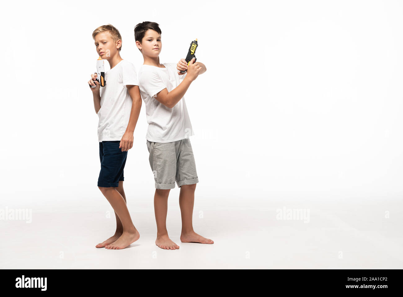 two brothers standing back to back, holding toy guns and looking at ...