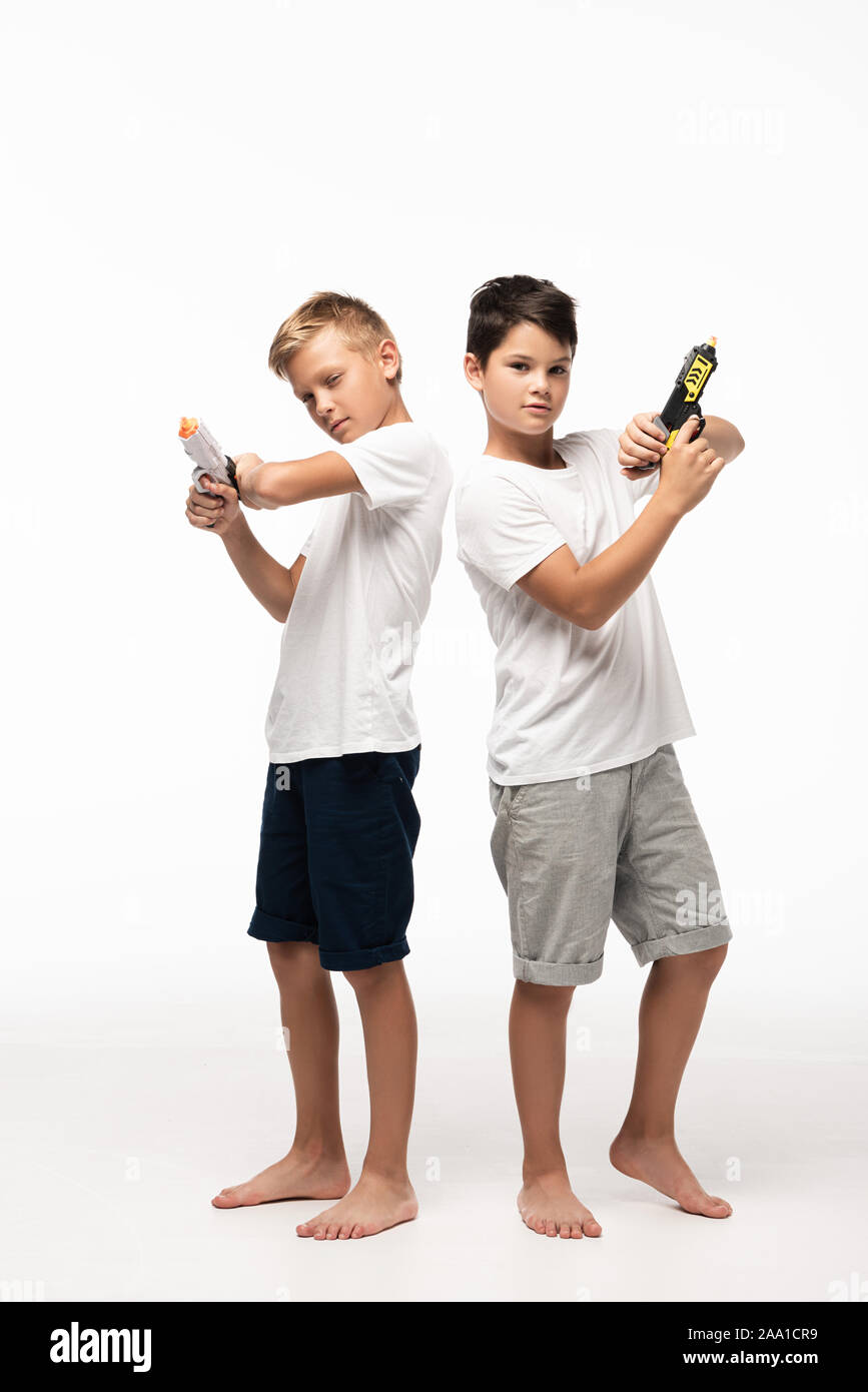 two brothers standing back to back, holding toy guns and looking at ...
