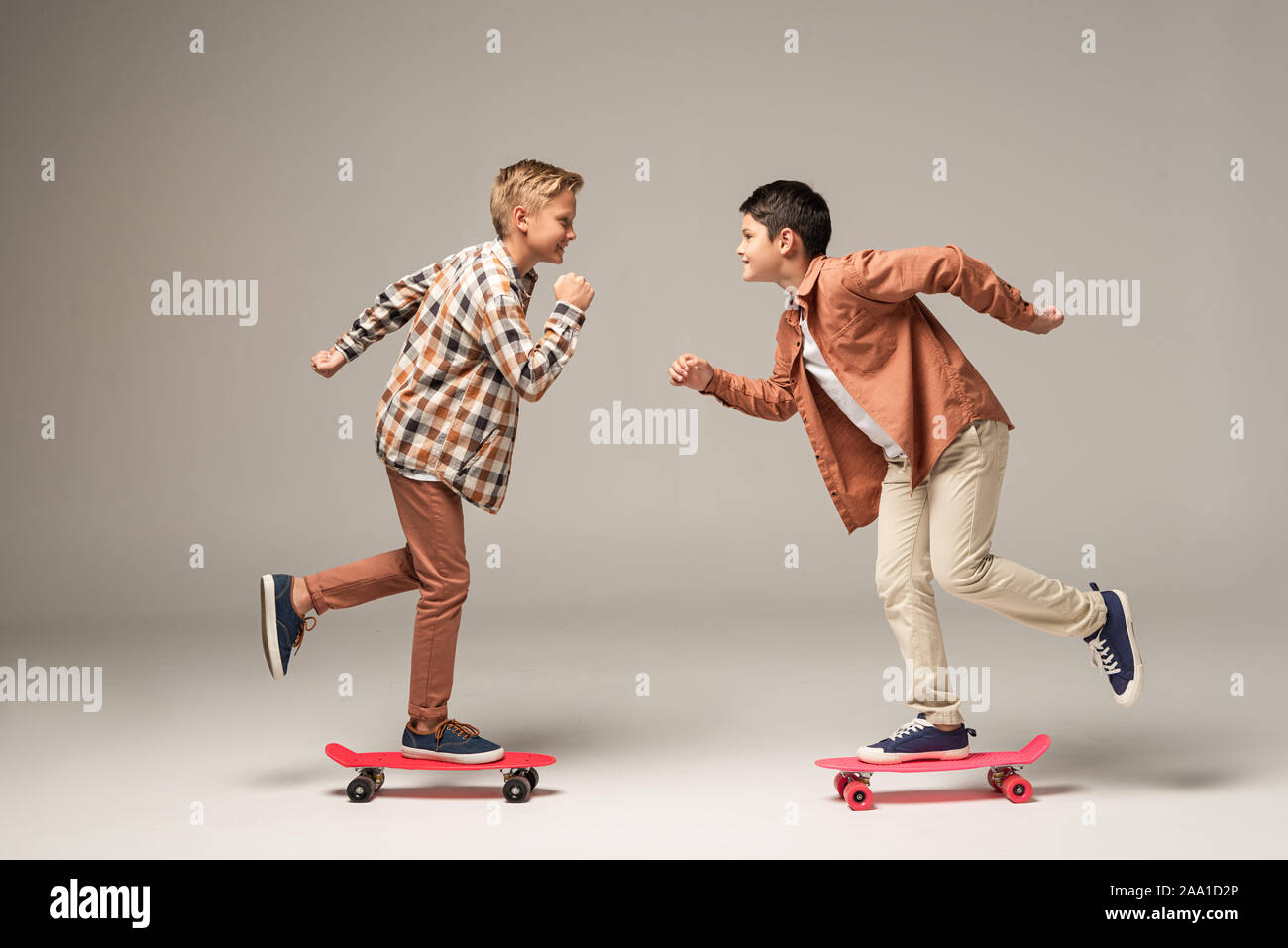 side view of two cheerful brothers riding penny boards while looking at ...
