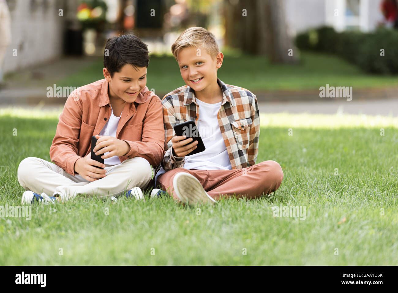 two smiling brothers sitting on green grass and using smartphones Stock ...