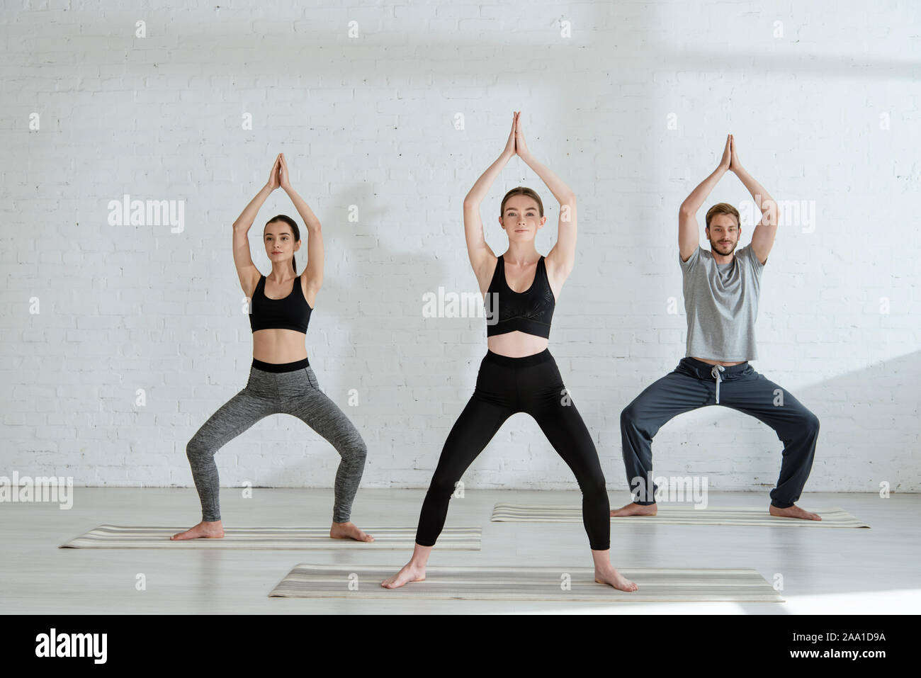 young men and woman practicing yoga in goddess pose with raised prayer ...