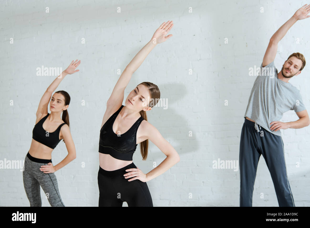 young people in sportswear doing side tilt in mountain pose with hand ...