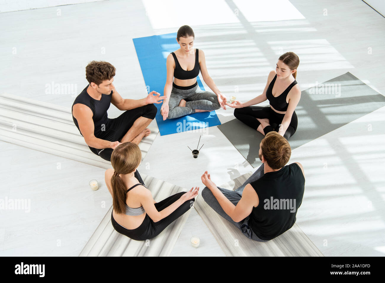 five young people sitting in circle and meditating in easy pose near ...