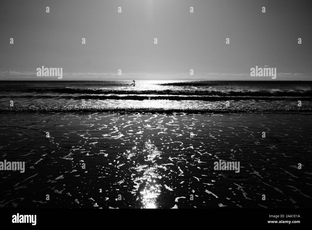 A surfboarder negotiates the light surf in a pool of bright winter ...