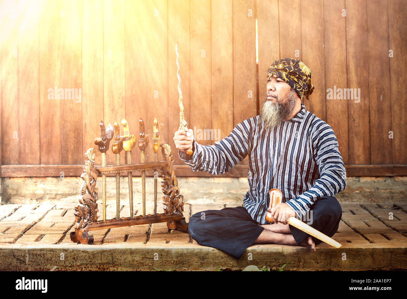 Asian old man showing his keris or kris collection with wooden wall ...