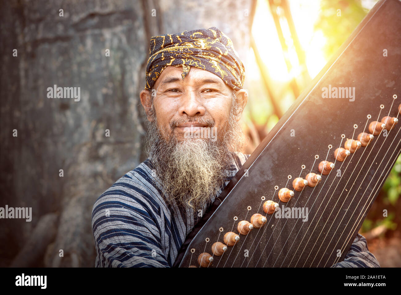 Asian old man holding kecapi with tree background. Kecapi is a ...