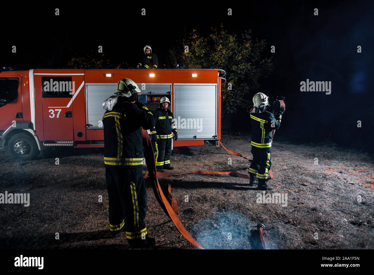 Group of firemen putting out a fire with a long water hose Stock Photo ...